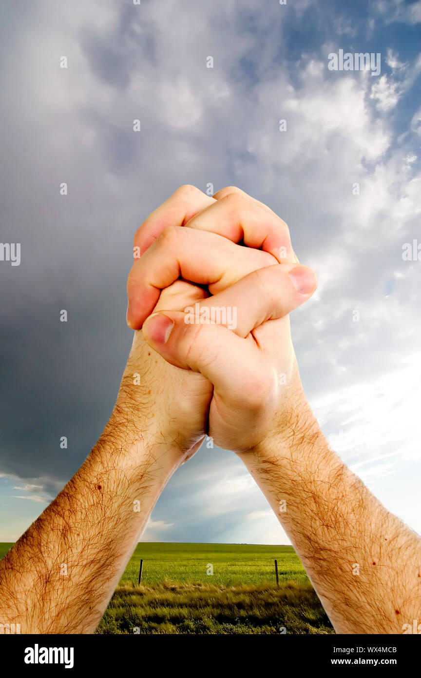 A pair of hands praying with a prairie landscape with rain clouds in ...