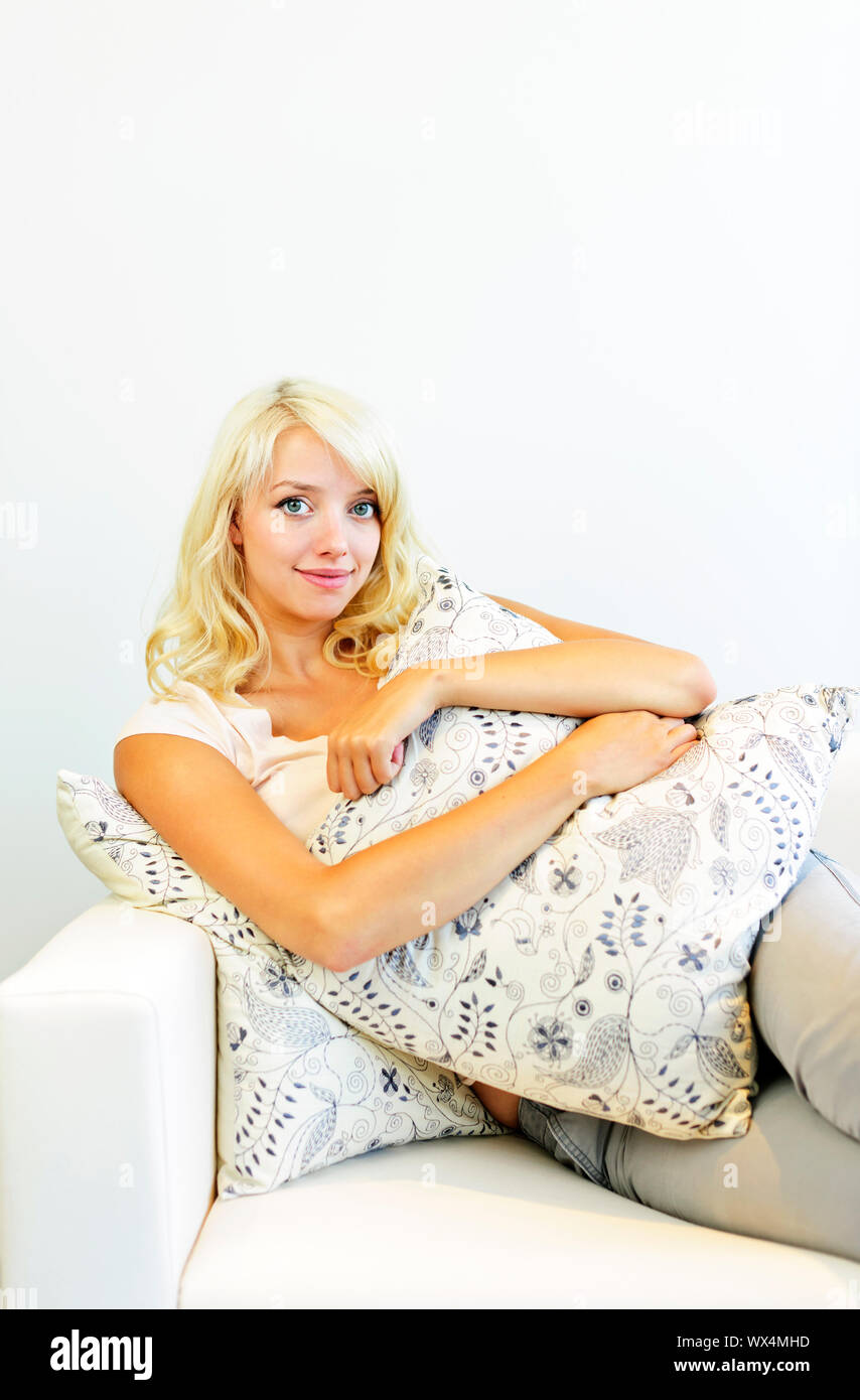 Beautiful blonde woman hugging cushion on couch and relaxing at home ...