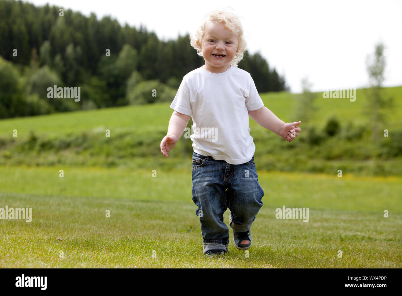 A cute smiling child running and playing outdoors in grass Stock Photo ...
