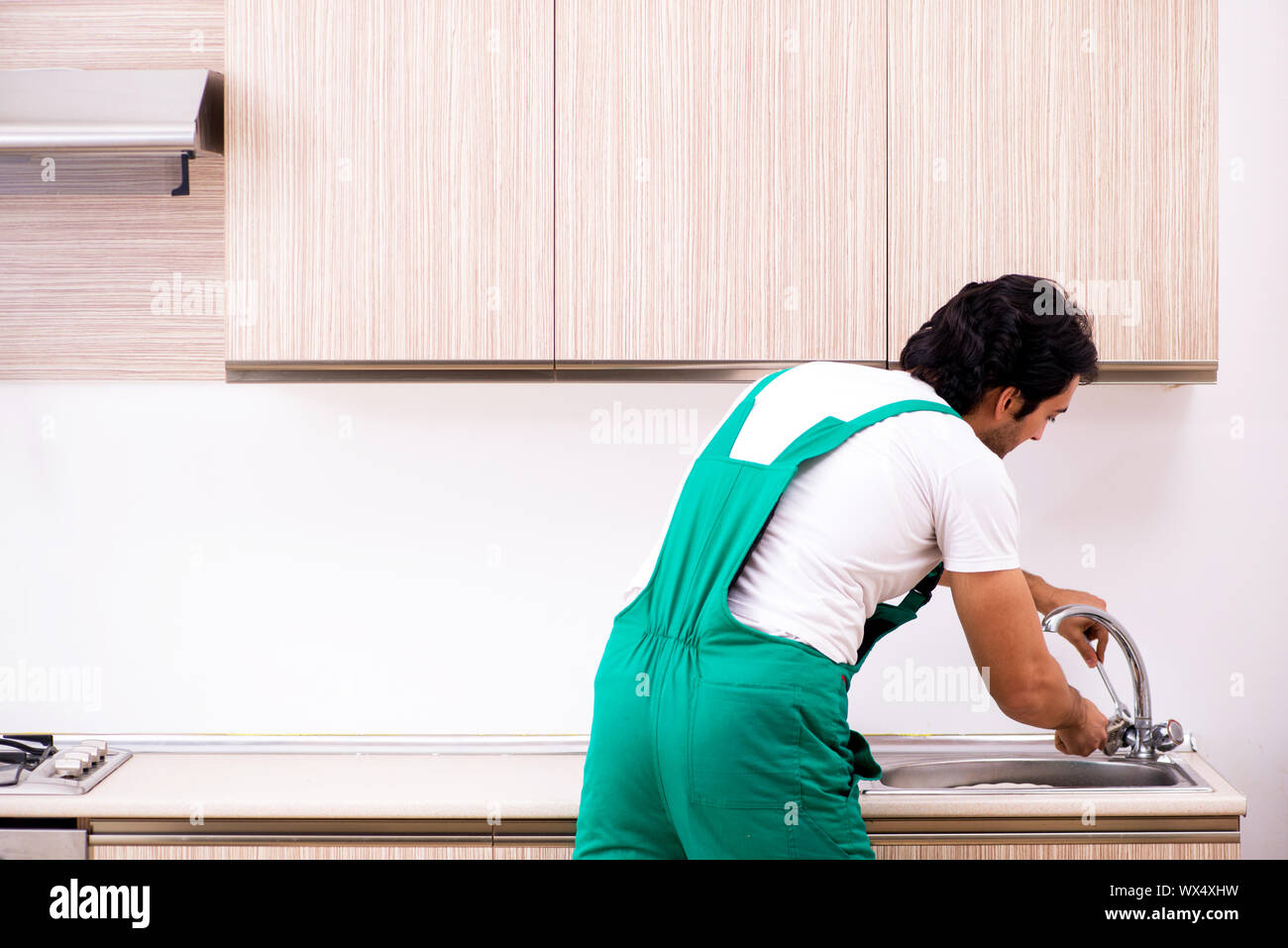 Young plumber repairing tap at kitchen Stock Photo - Alamy