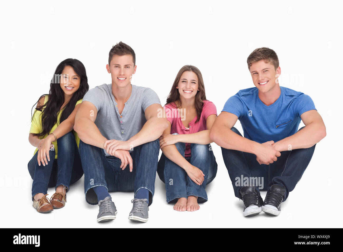 A smiling group of friends sitting beside each other on the ground with ...