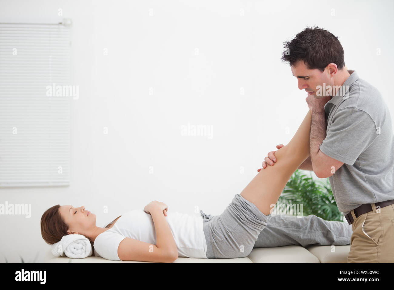 Chiropractor massaging a leg while placing it on his shoulder in a room ...
