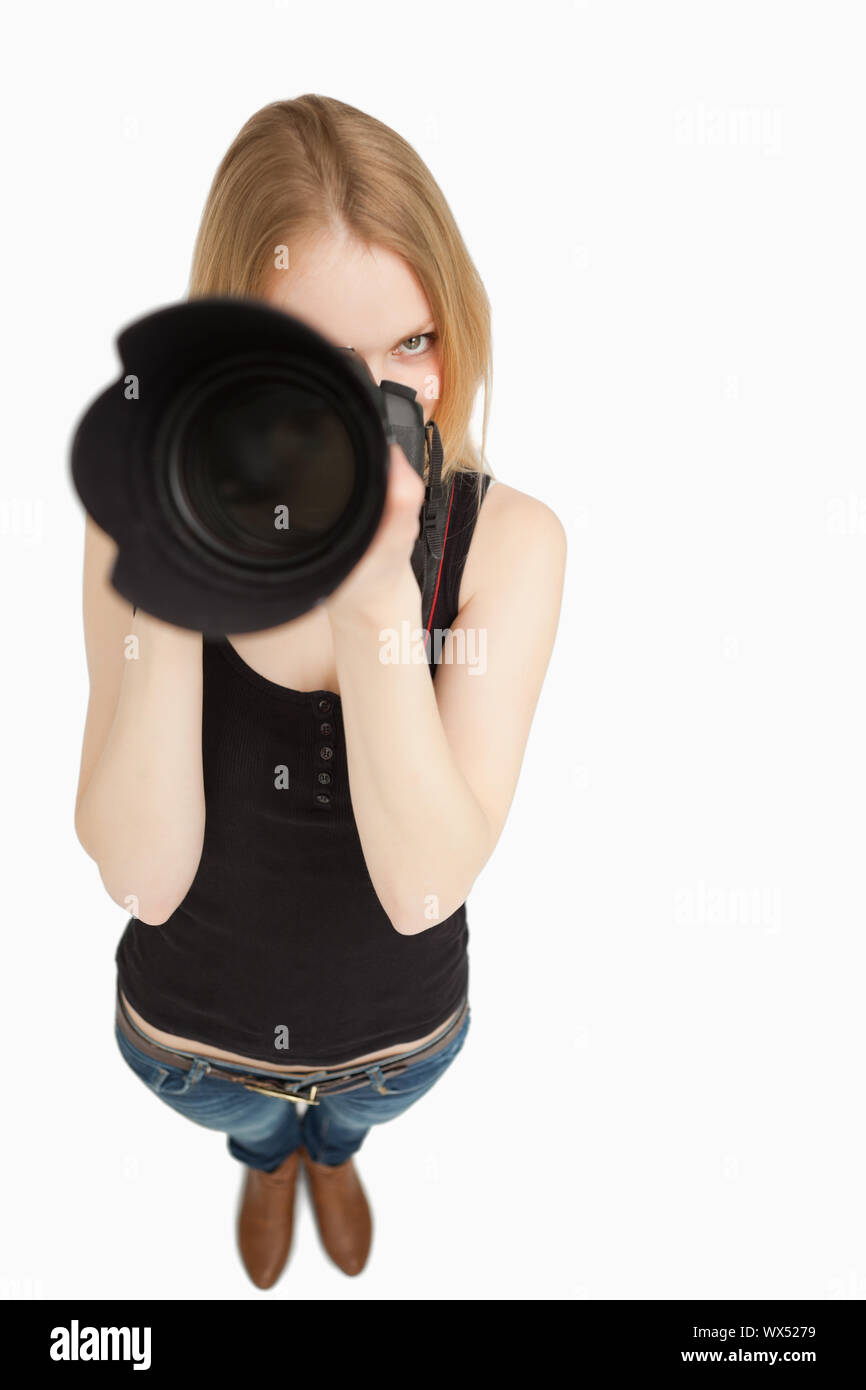 Blonde-haired girl aiming with her SLR camera against white background ...