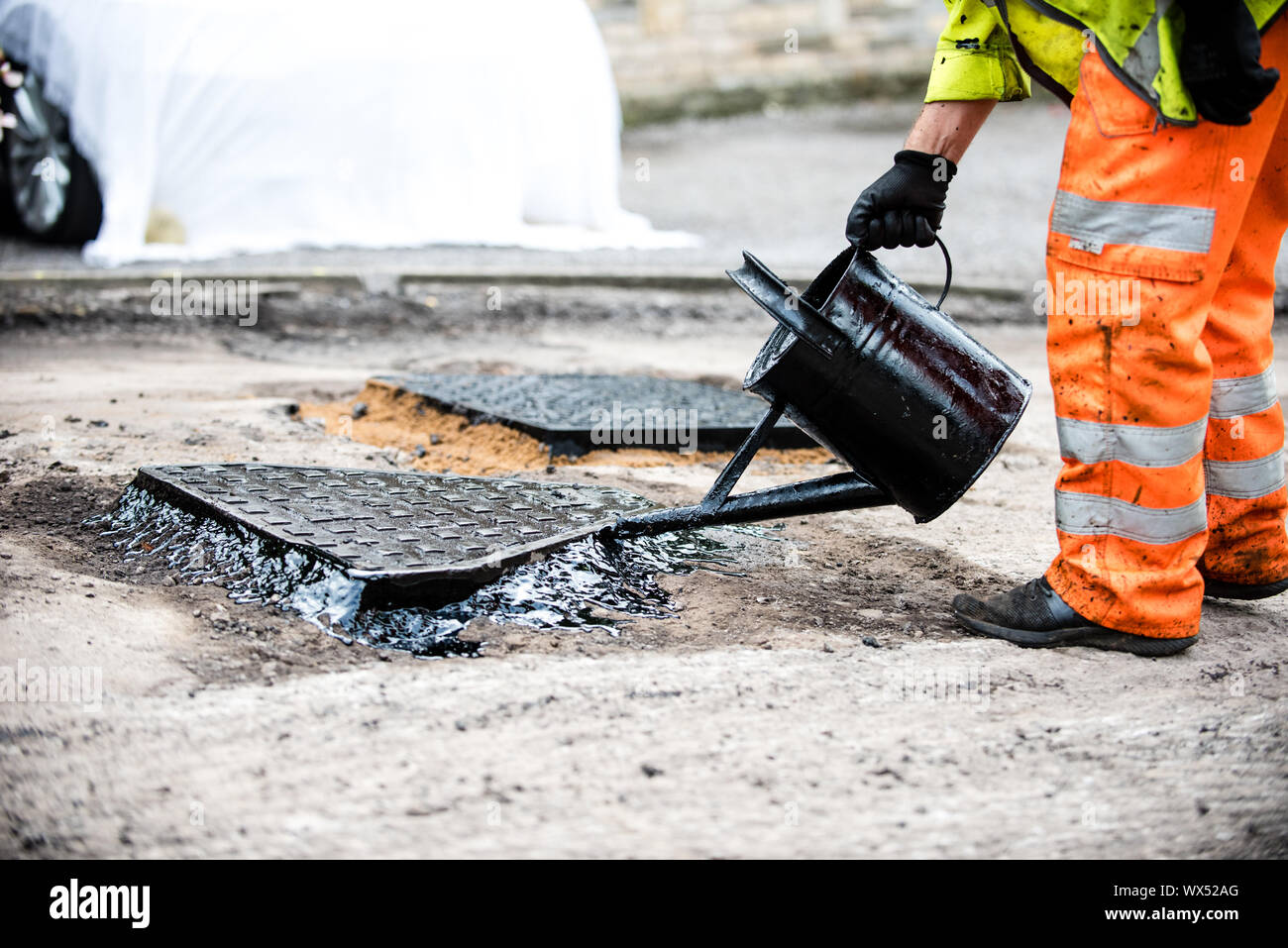 Man pours tar from a watering can around a manhole cover on a road ...