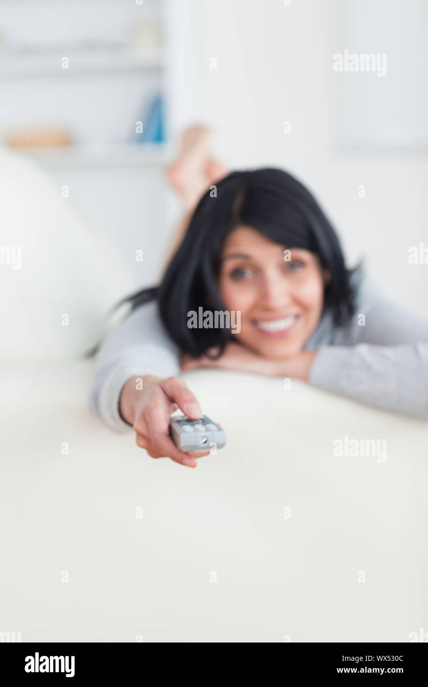 Woman pressing on a remote control while laying on a sofa in a living ...