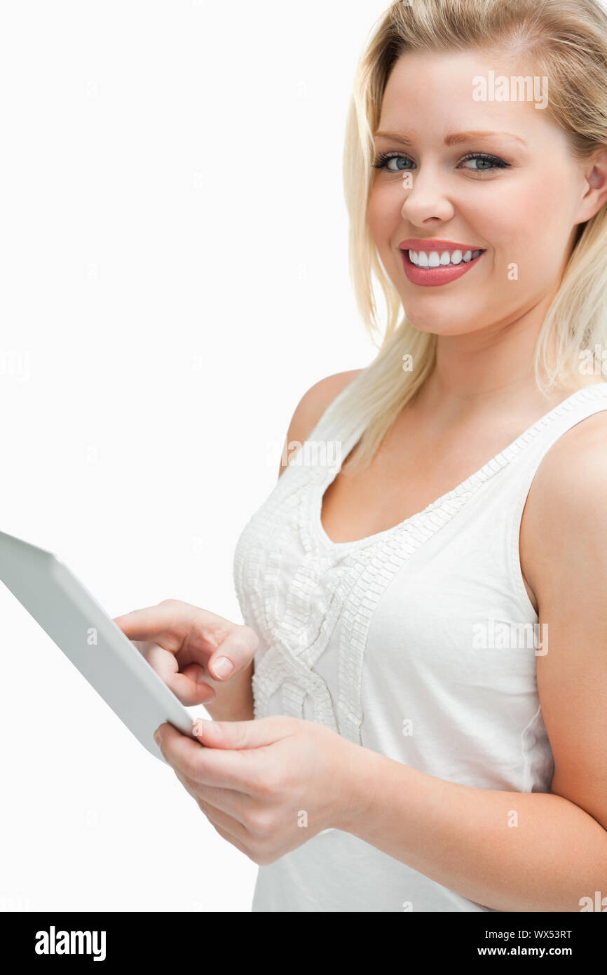 Cheerful blonde woman touching her tablet computer against a white ...