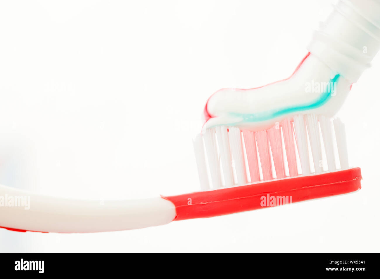 Red toothbrush with multicolour toothpaste against white background ...