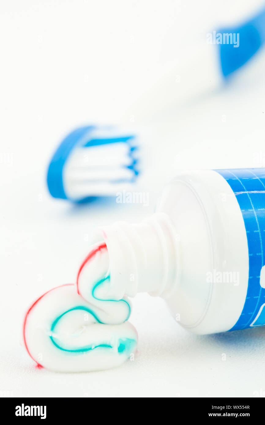 Blue toothpaste tube next to a toothbrush against white background ...