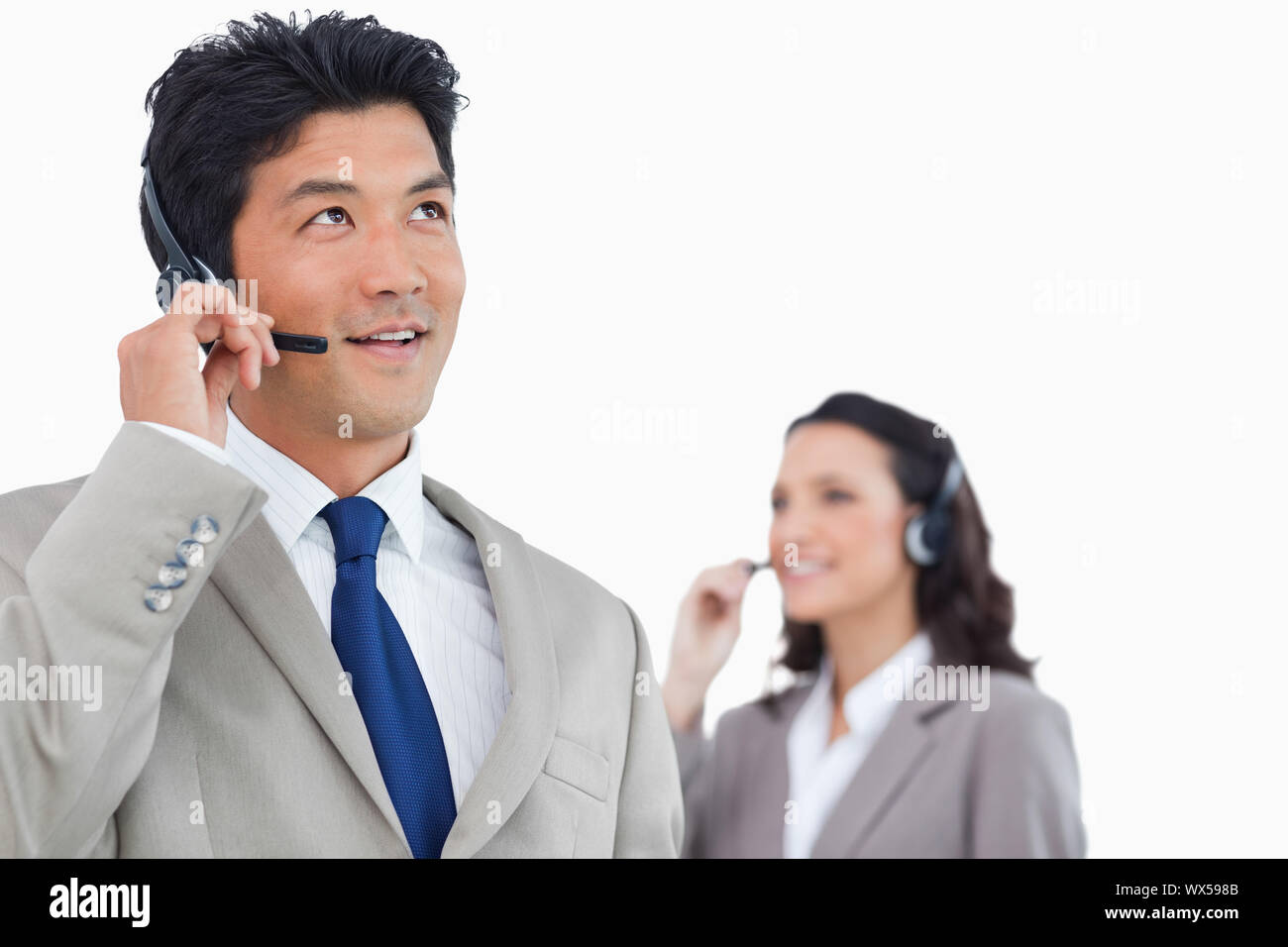 Call center agent with headset and colleague behind him against a white ...