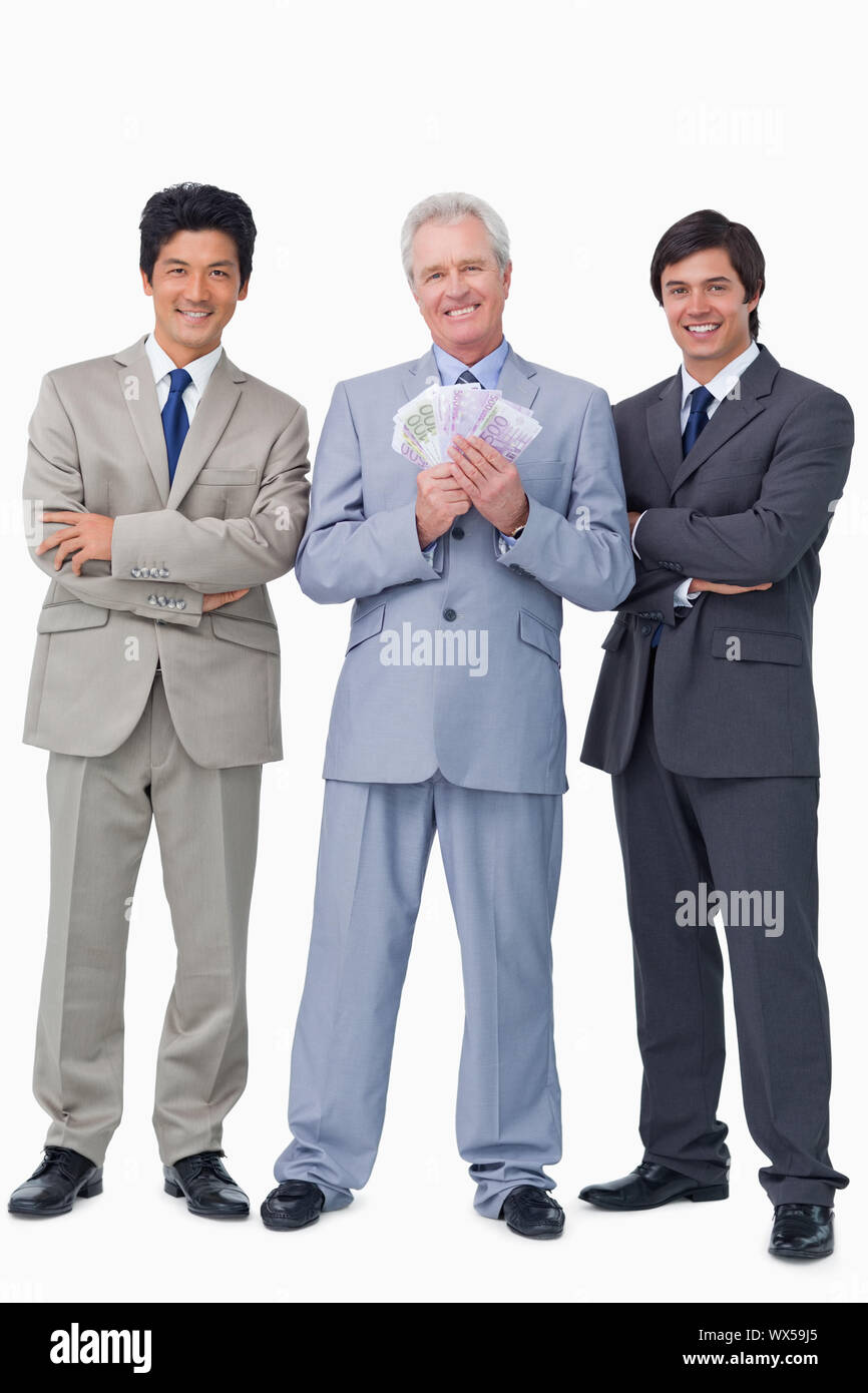 Smiling senior salesman with money and employees against a white ...