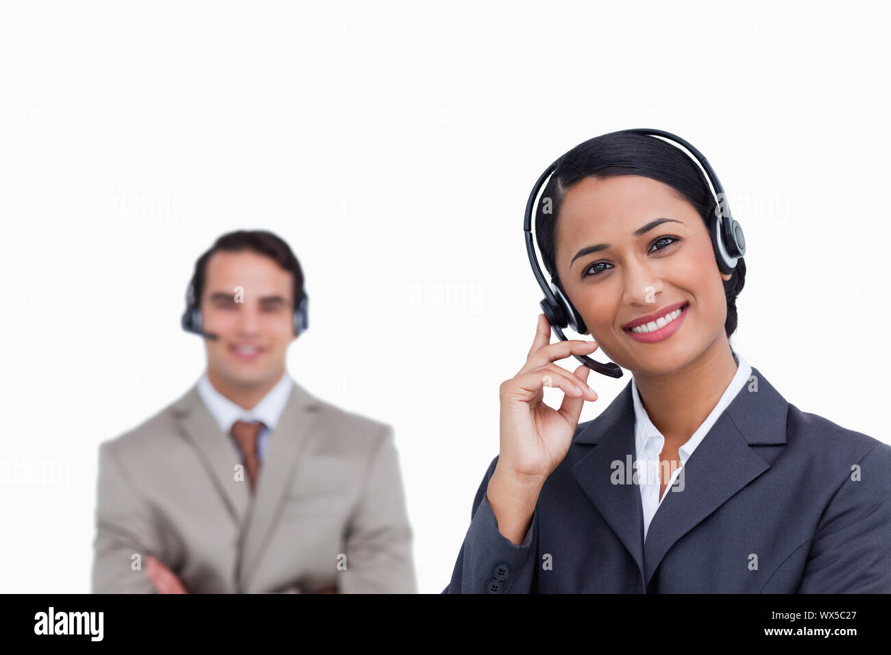 Smiling telephone support employee with co-worker behind her against a ...