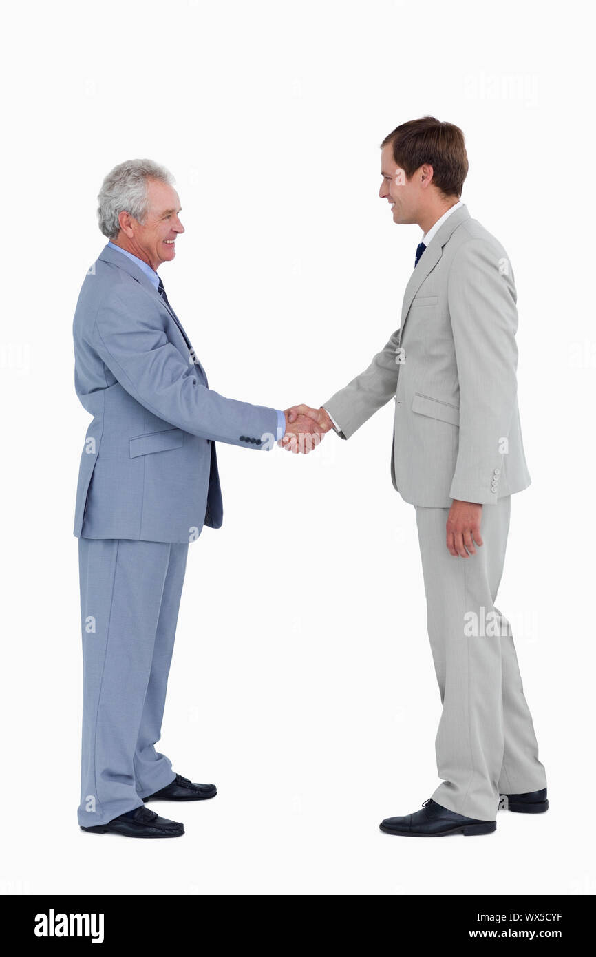 Side view of smiling tradesmen shaking hands against a white background ...