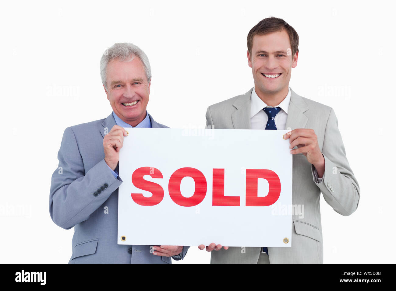 Smiling real estate agents holding sold sign against a white background ...