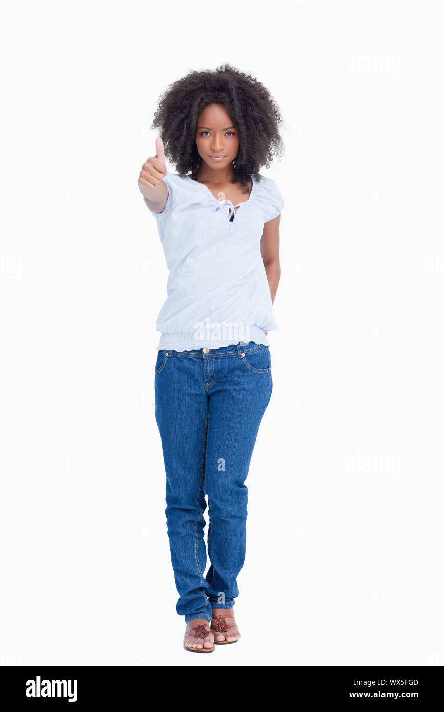 Young woman seriously standing upright with her thumbs up and a hand on ...