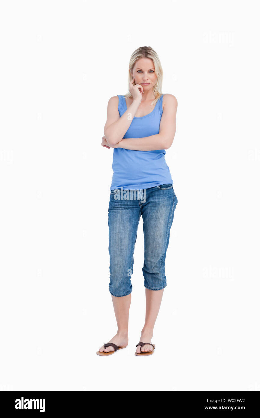 Blonde woman standing up with finger on her cheek against a white ...