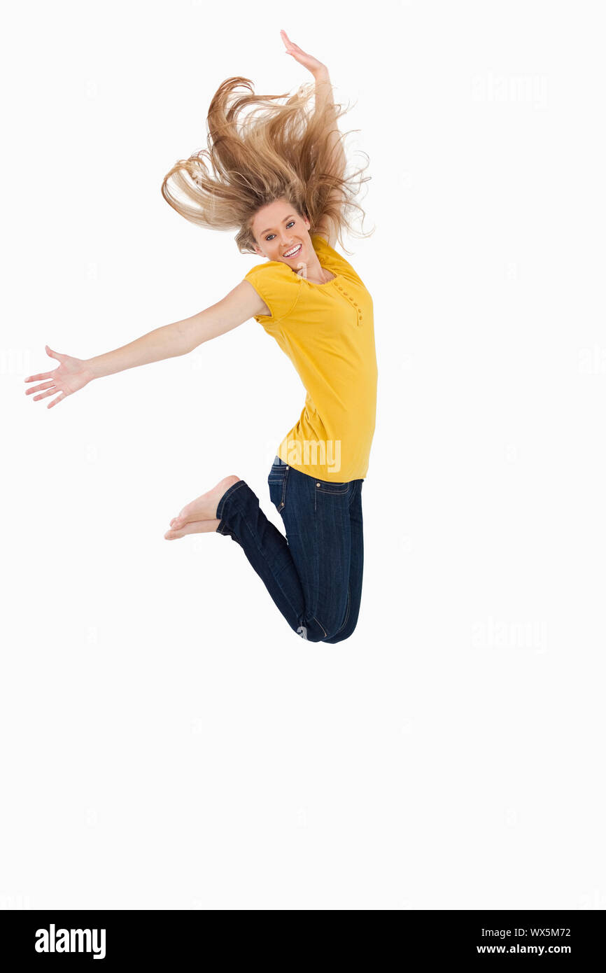 Blonde woman in yellow shirt jumping against white background Stock ...
