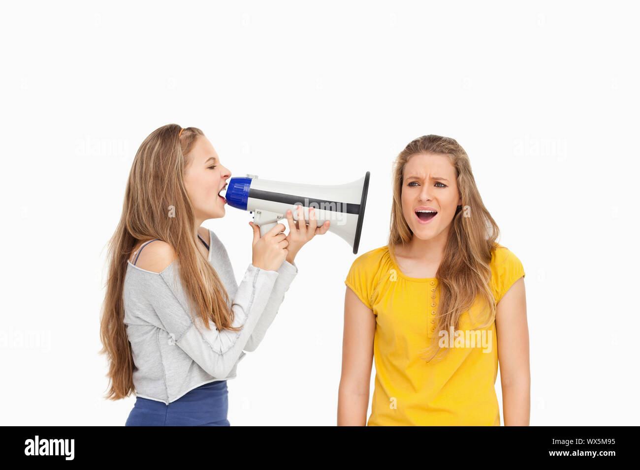 Female student using a loudspeaker on a other girl against white ...