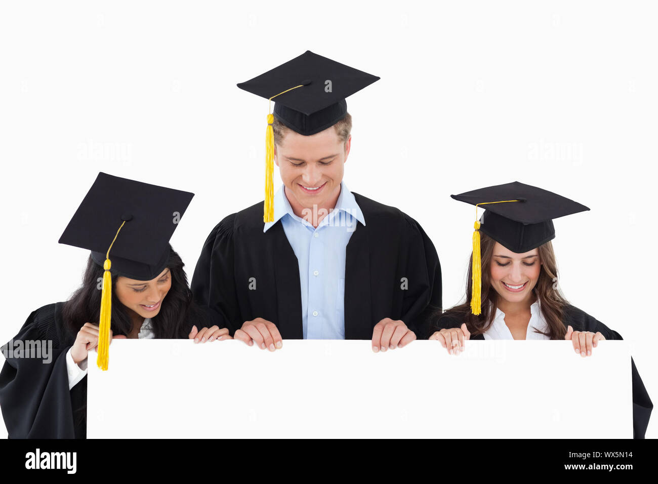 Three graduates holding a blank sheet as they look down at it and ...