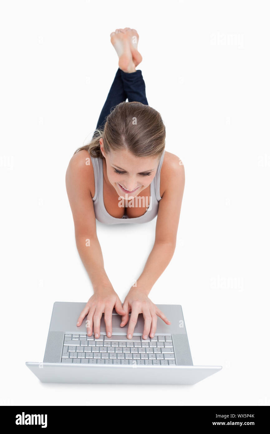 Portrait of a woman using a laptop while lying on the floor against a ...