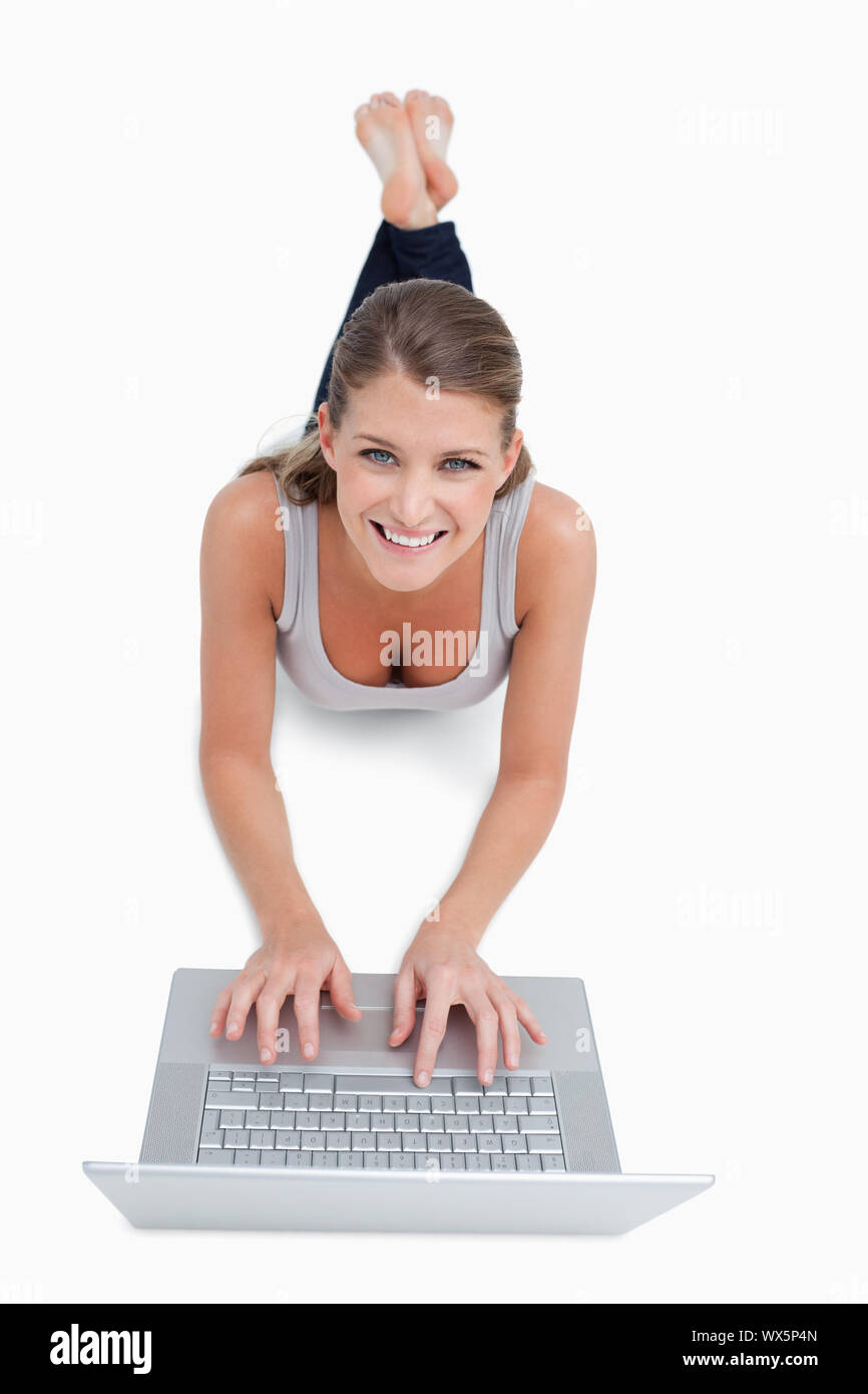 Portrait of a woman using a notebook while lying on the floor against a ...