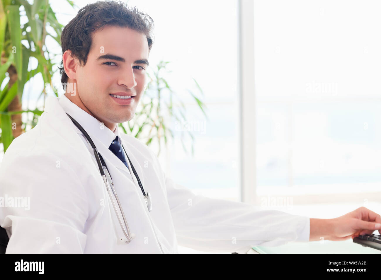 Side view of young doctor sitting behind his desk Stock Photo - Alamy
