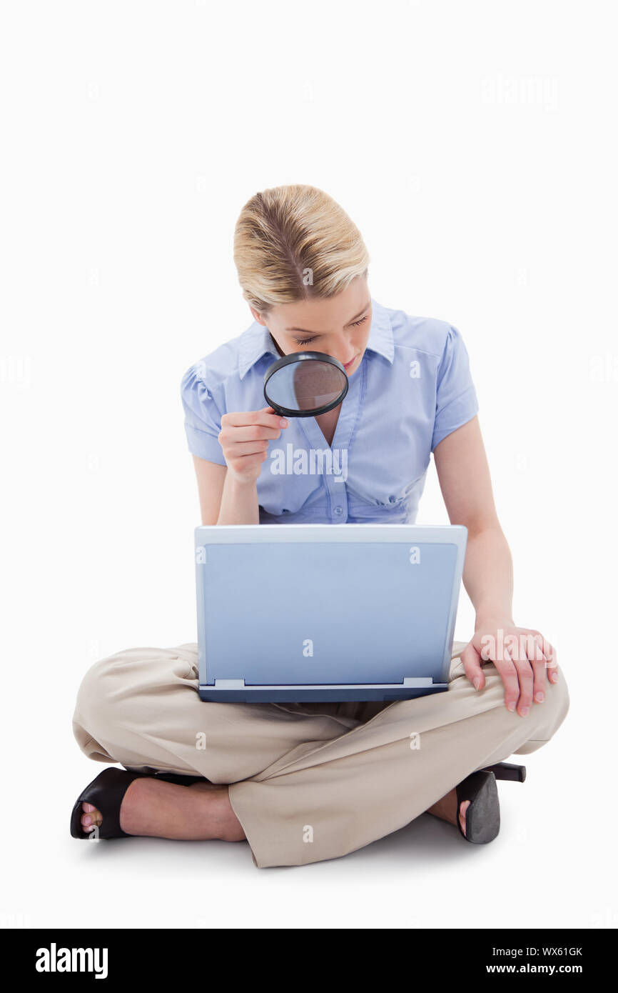 Woman using magnifier to look at her laptop against a white background ...