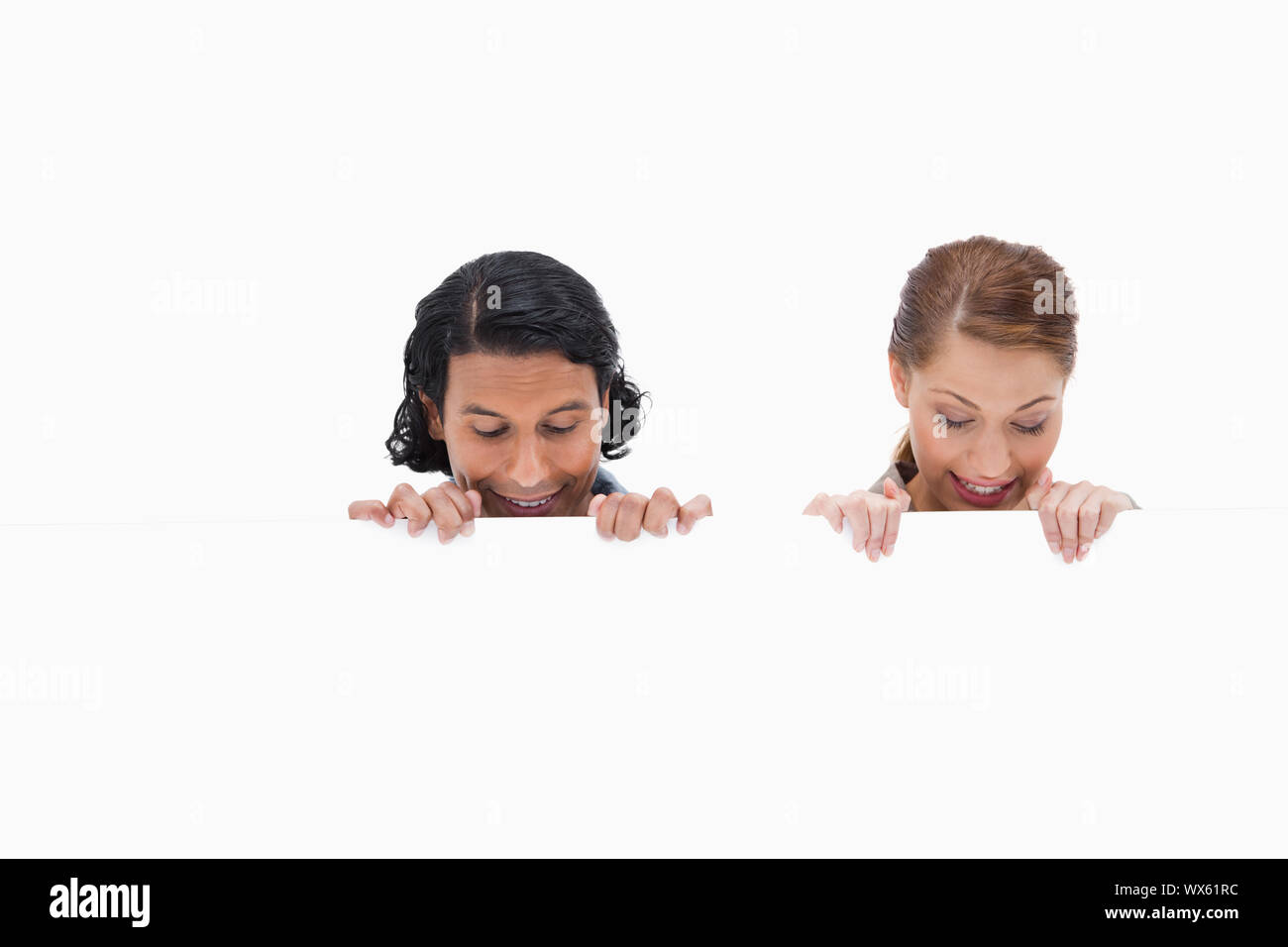 Cheerful couple looking down on blank wall against a white background ...