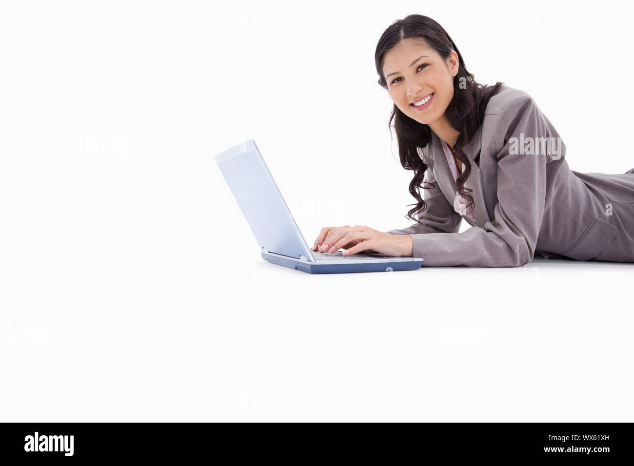 Side view of smiling woman lying while working on laptop against a ...