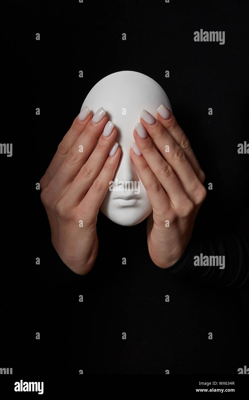 Girl's hands close eyes of plaster mask face on a black background. See ...