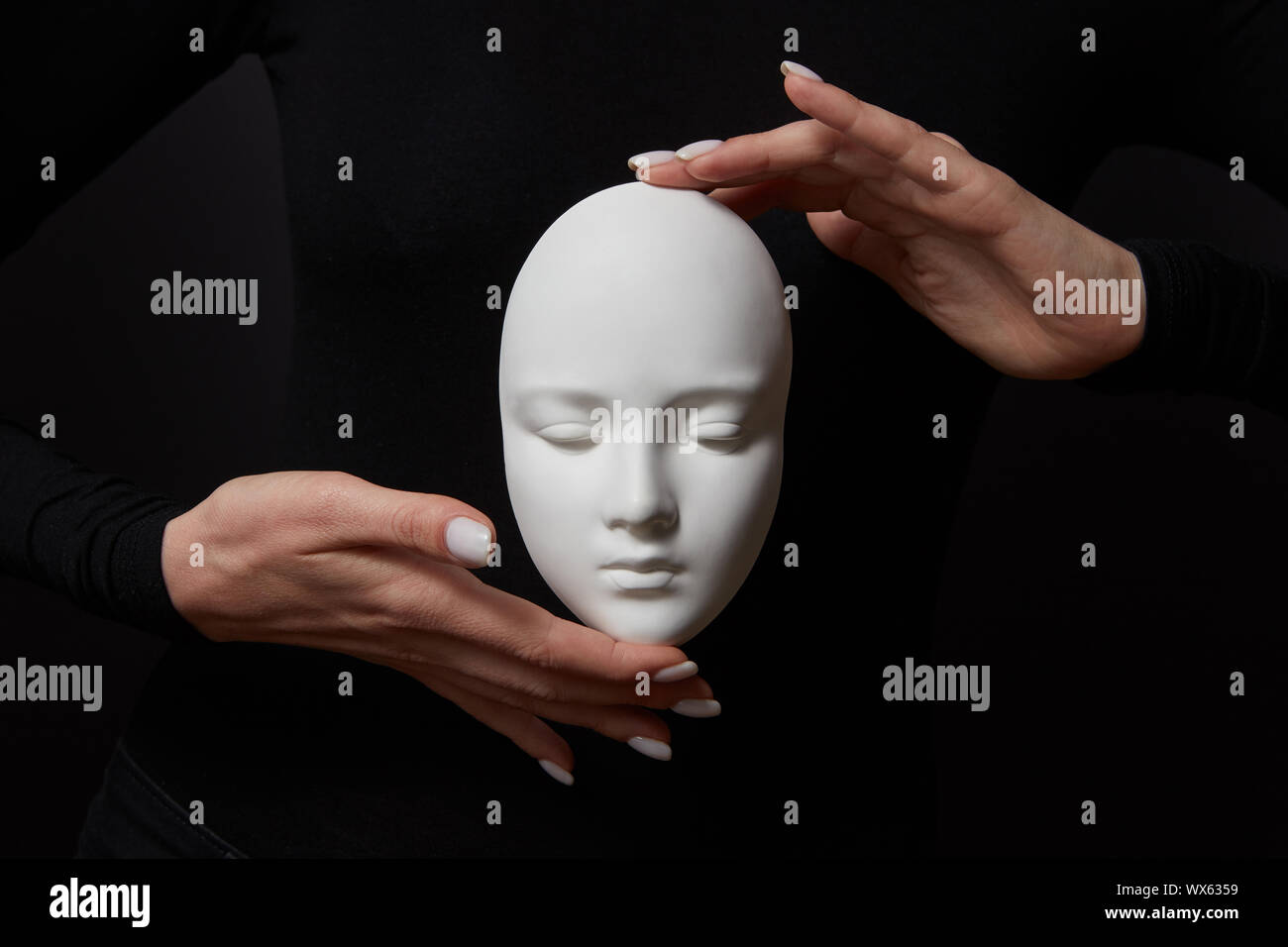 Two woman's hands hold white gypsum mask face on a black background ...