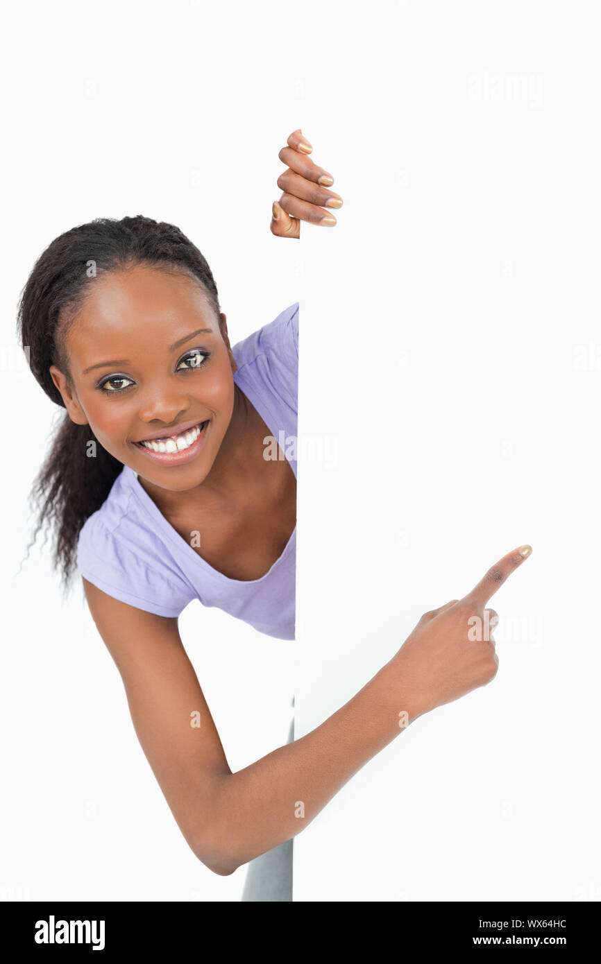 Young smiling woman looking around the corner pointing at something on ...