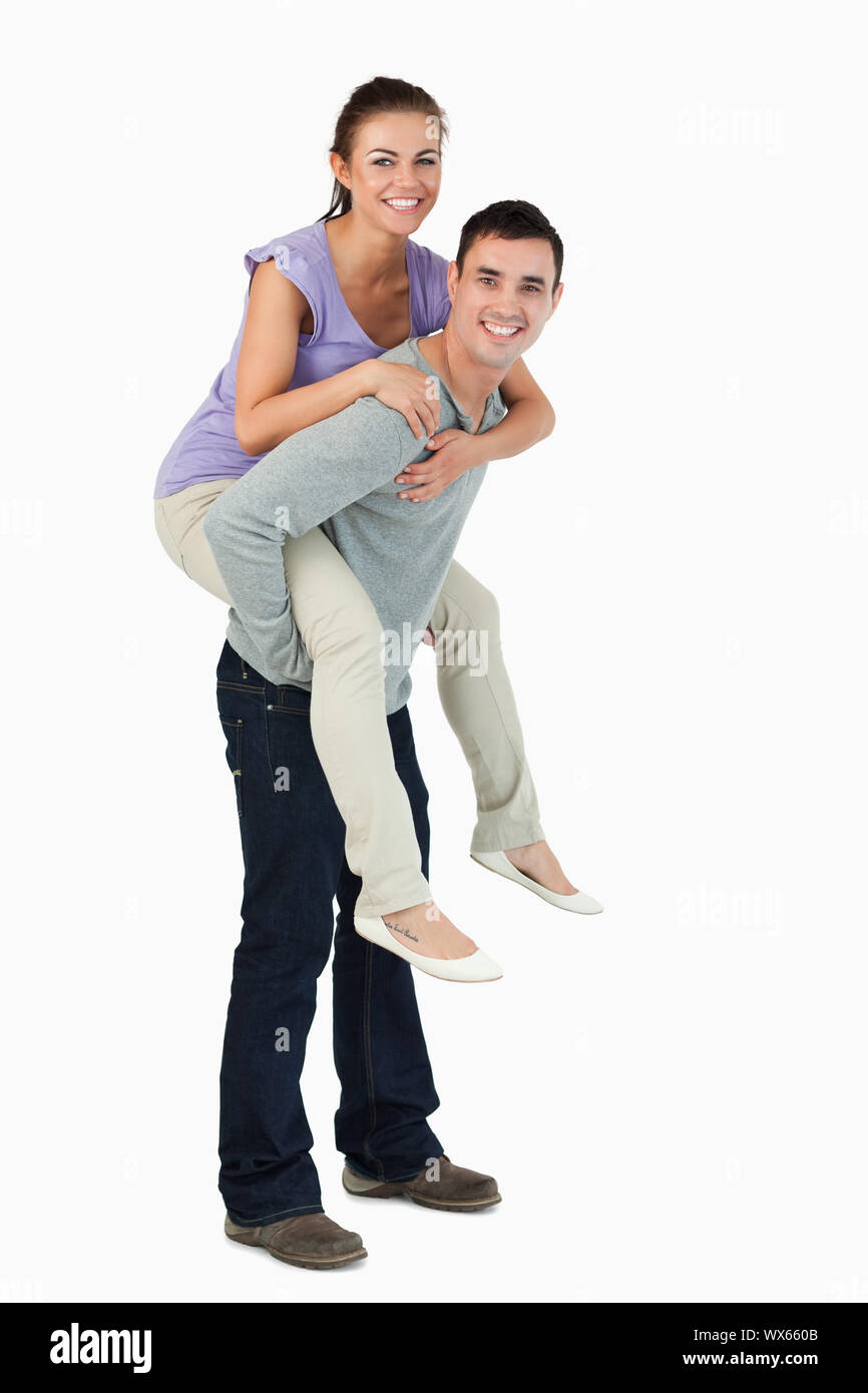 Young male carrying his girlfriend piggyback against a white background ...