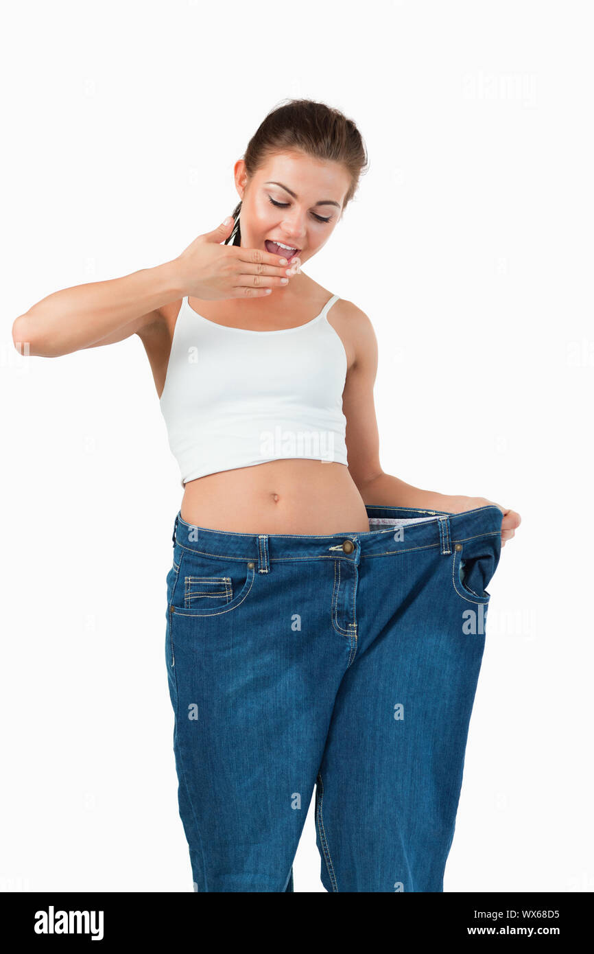 Portrait of a suprised woman wearing too large jeans against a white ...