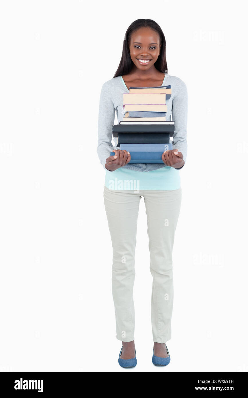Smiling young woman carrying a stack of books against a white ...