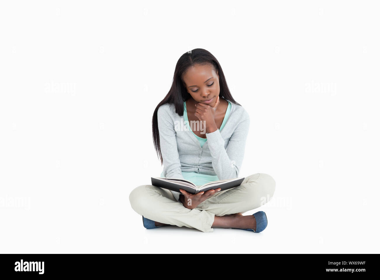 Young woman sitting on the floor reading in her book against a white ...