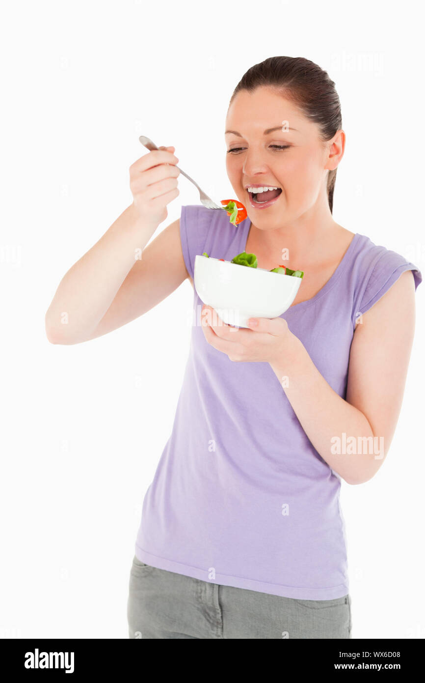 Beautiful woman eating a bowl of salad while standing against a white ...