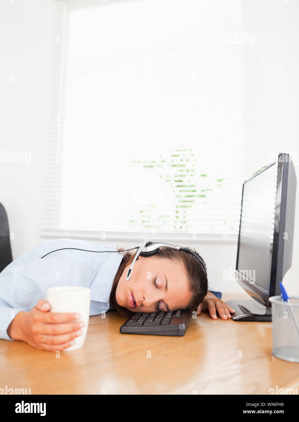 A secretary with a headset and a cup of coffee sleeps in an office ...