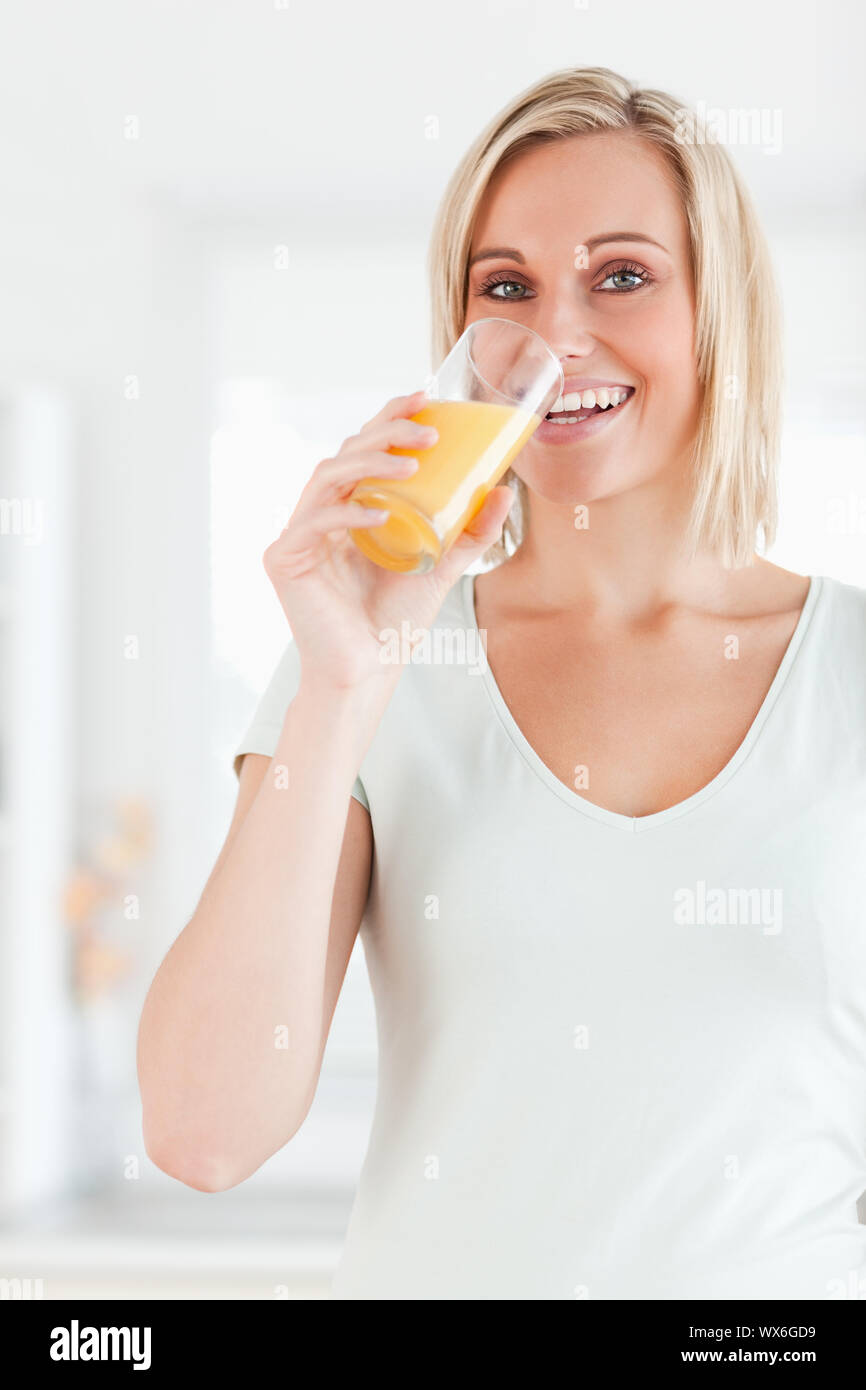 Cute woman drinking orange juice looking into the camera in the kitchen ...
