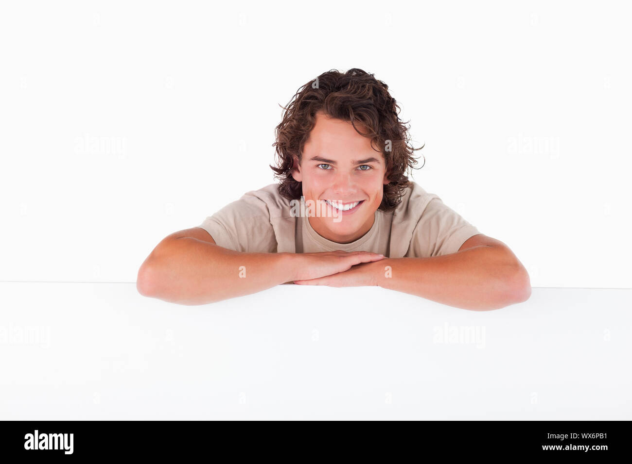 Smiling man leaning on a whiteboard looking into the camera in a studio ...