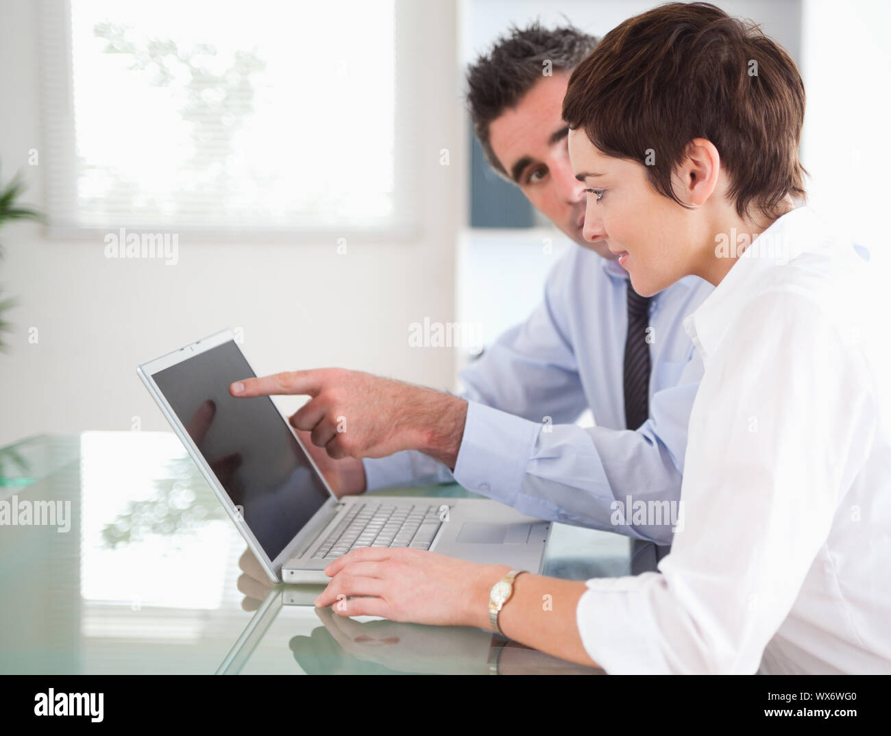 Man pointing at something to his secretary on a laptop in an office ...