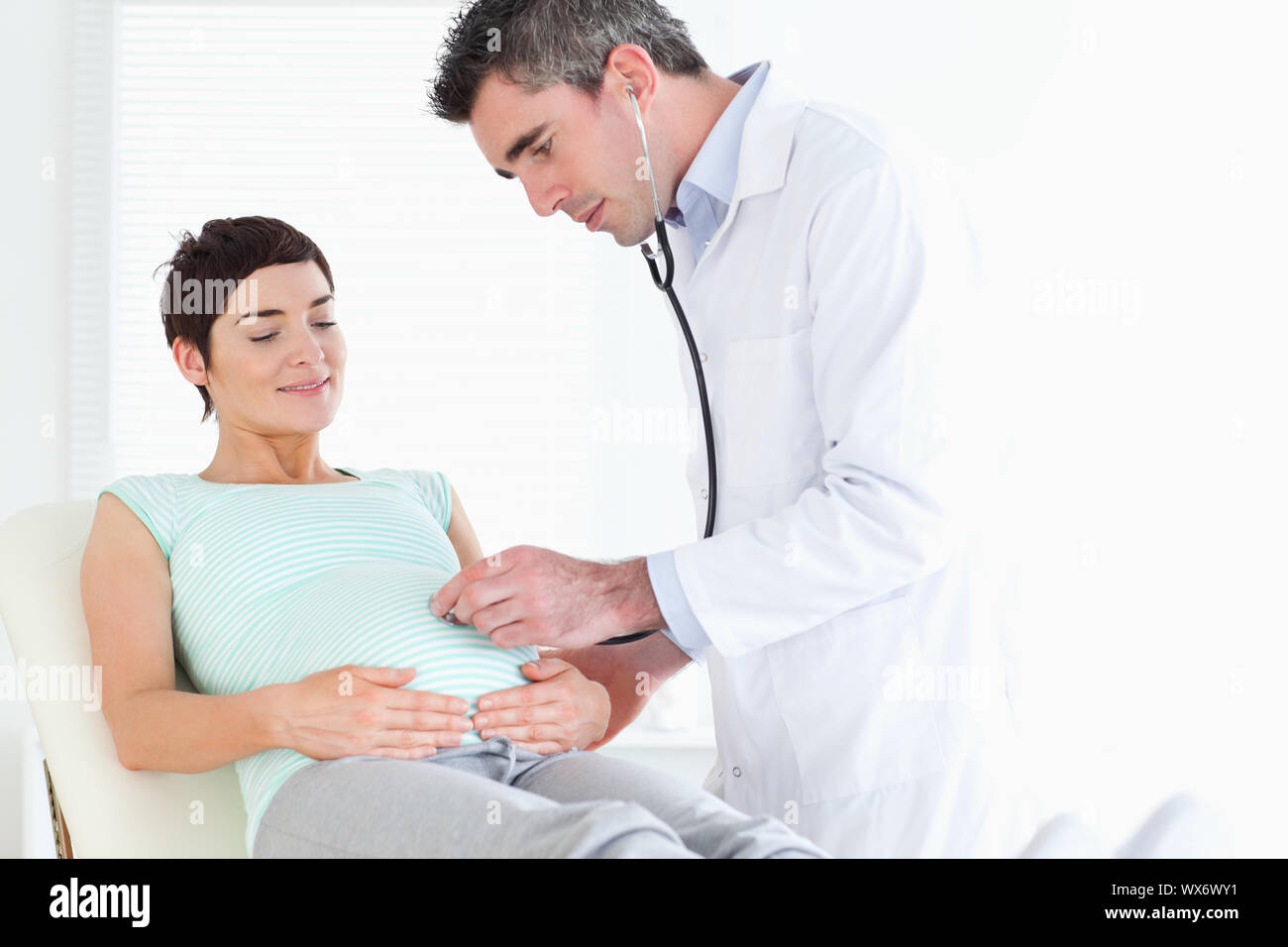 Doctor listening into the woman's tummy with a stethoscope in a room ...