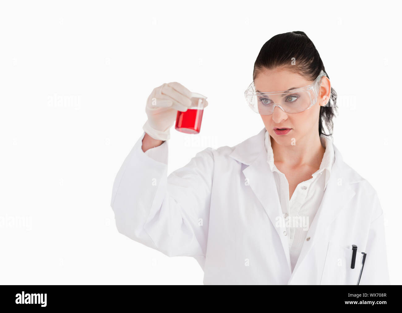 Dark-haired scientist with safety glasses looking at a red beaker in a ...