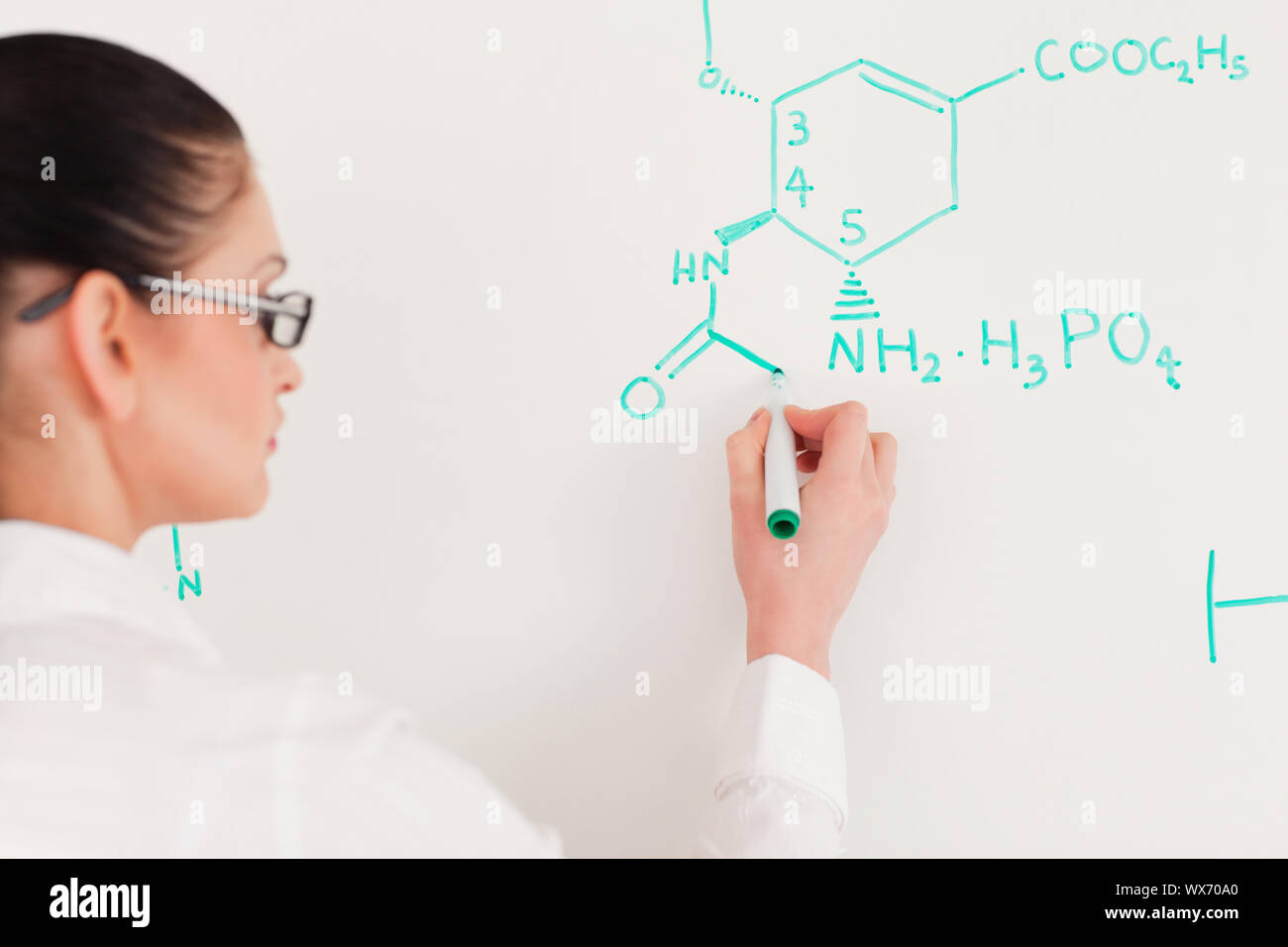 Dark-haired scientist woman writing a formula on a white board in a lab ...