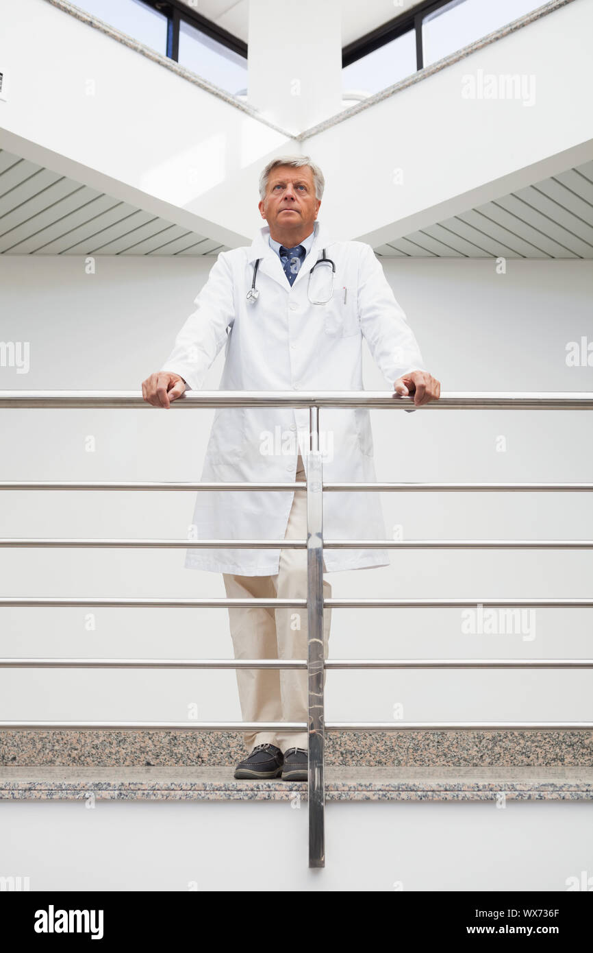 Thinking doctor stands at railing looking up in hospital corridor Stock ...