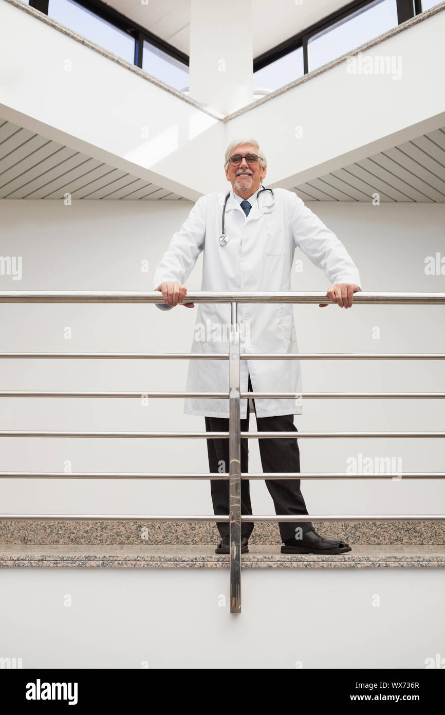 Happy doctor leans against rail in hospital corridor Stock Photo - Alamy