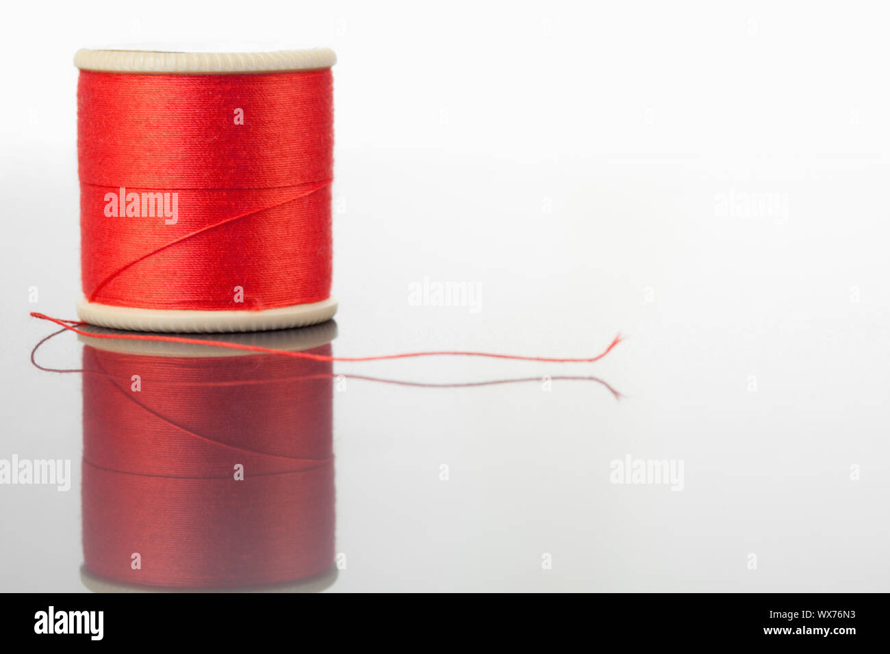 Red spool of thread on a table against a white background Stock Photo ...