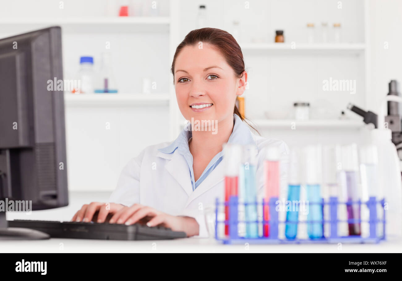 Red-haired scientist typing a report with her computer looking at the ...