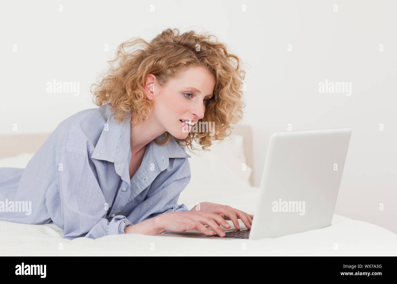 Gorgeous blonde woman relaxing with her laptop while lying on her bed ...