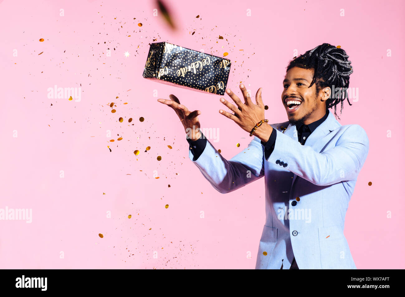 Excited man throwing gift in the air amid falling gold confetti Stock ...