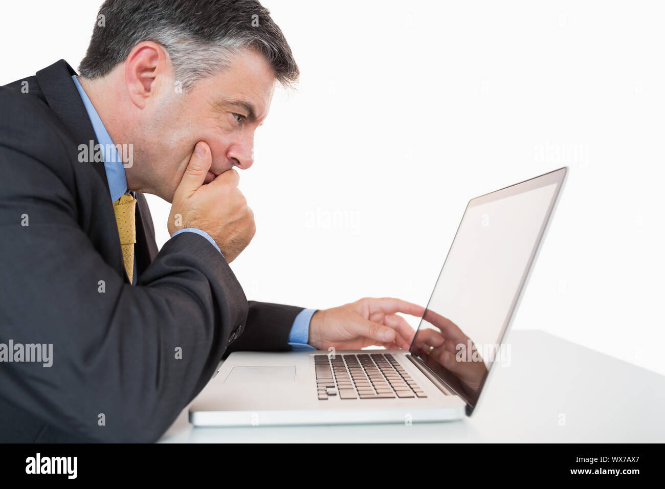 Thoughtful man typing on his laptop on his desk in a white background ...